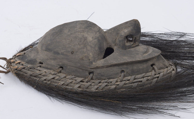 An ancestral mask, carved wood and natural fibre with feather fringe ...